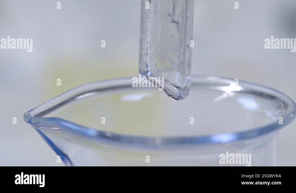 Close-up of liquid dripping from a pipette into a chemistry beaker ...