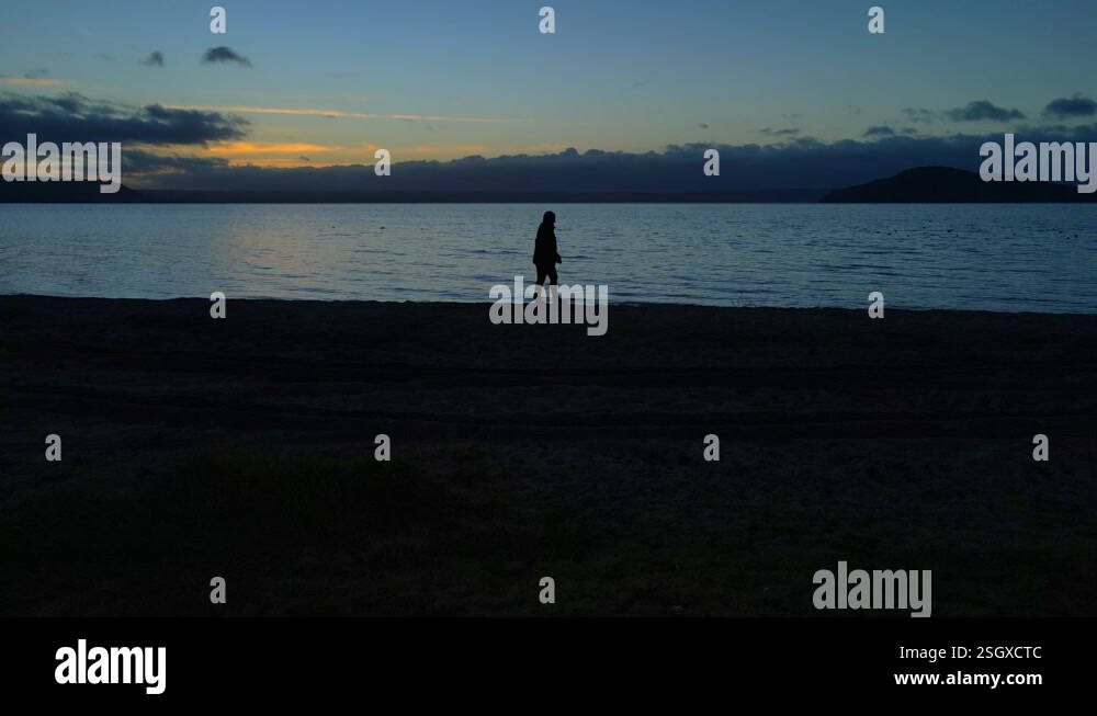 Lonely man slowly walking alone along shore at sunset with horizon in ...