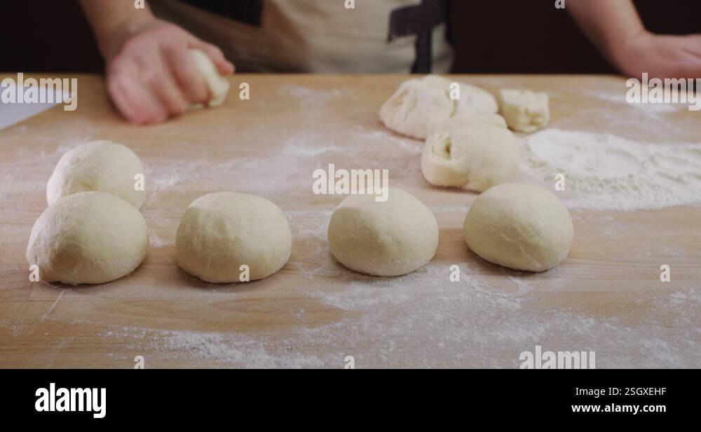 The baker rolls out the dough for buns on the board. Working in a ...