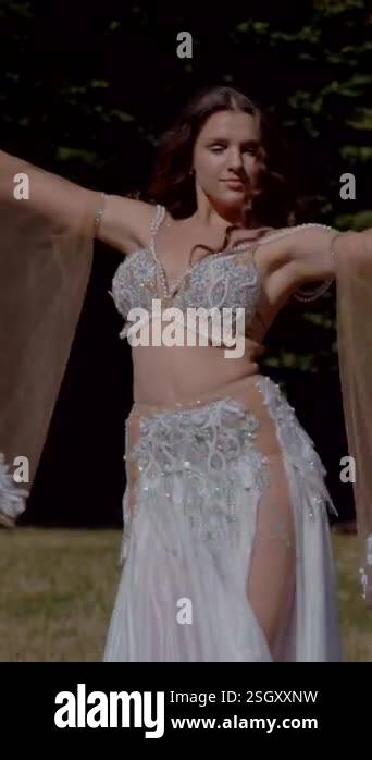 Vertical. Girl belly dancing in the forest. Oriental dance. Woman in white belly dance costume ...