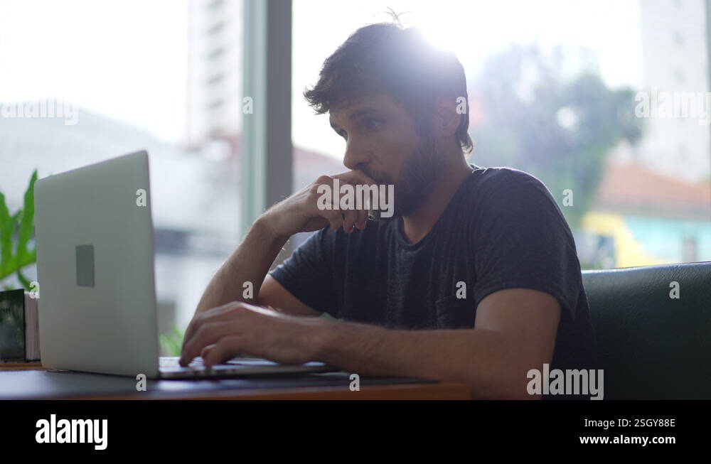 Young man staring at laptop screen seated at coffee shop. Concentrated ...