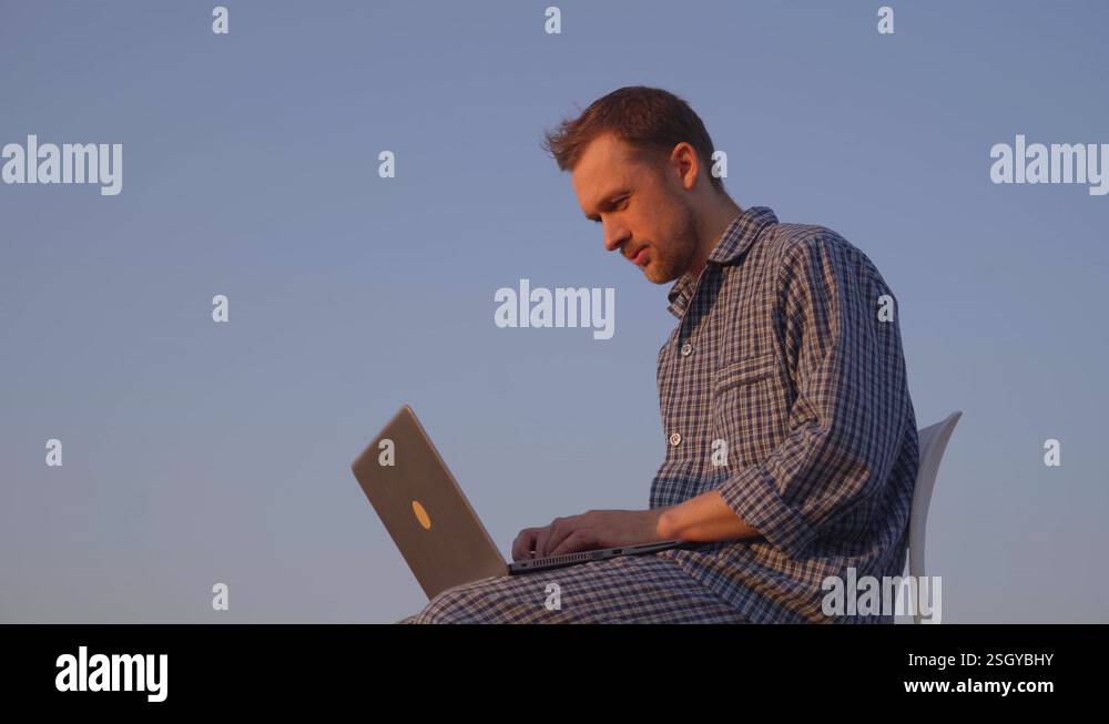 Caucasian freelancer man using laptop outdoor in pyjamas, hardly ...
