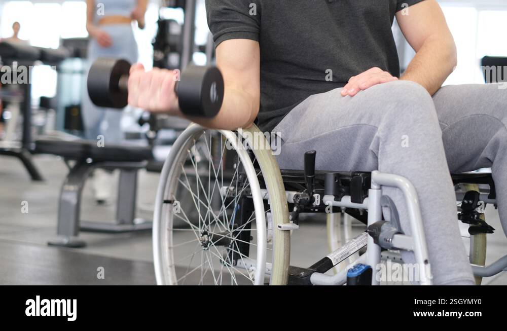A disabled man in a wheelchair exercises with dumbbells in the gym ...