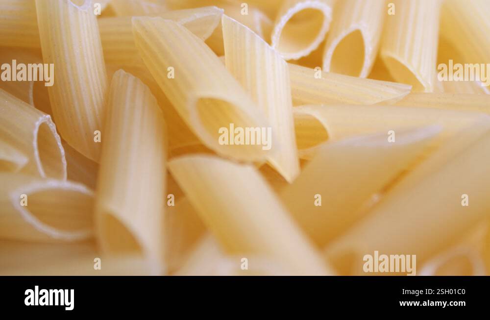 A pile of raw yellow pipe-shaped pasta lies on the surface. Raw pasta ...