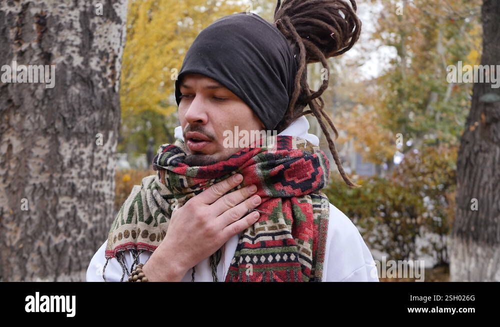 Attractive guy with dreadlocks sad and sick in a scarf touches his sore ...