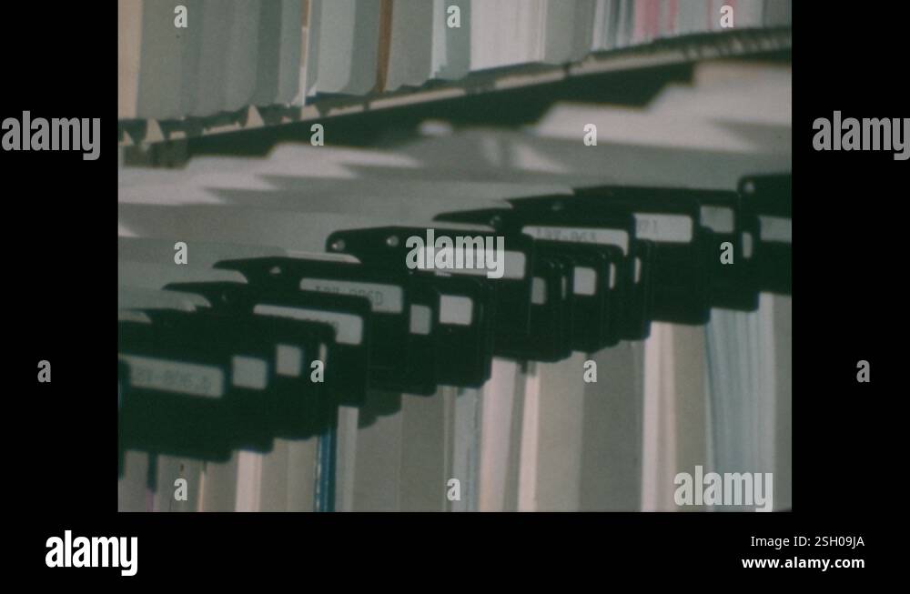 1960s: Indexed file folders hang on racks. Hand removes index card with ...