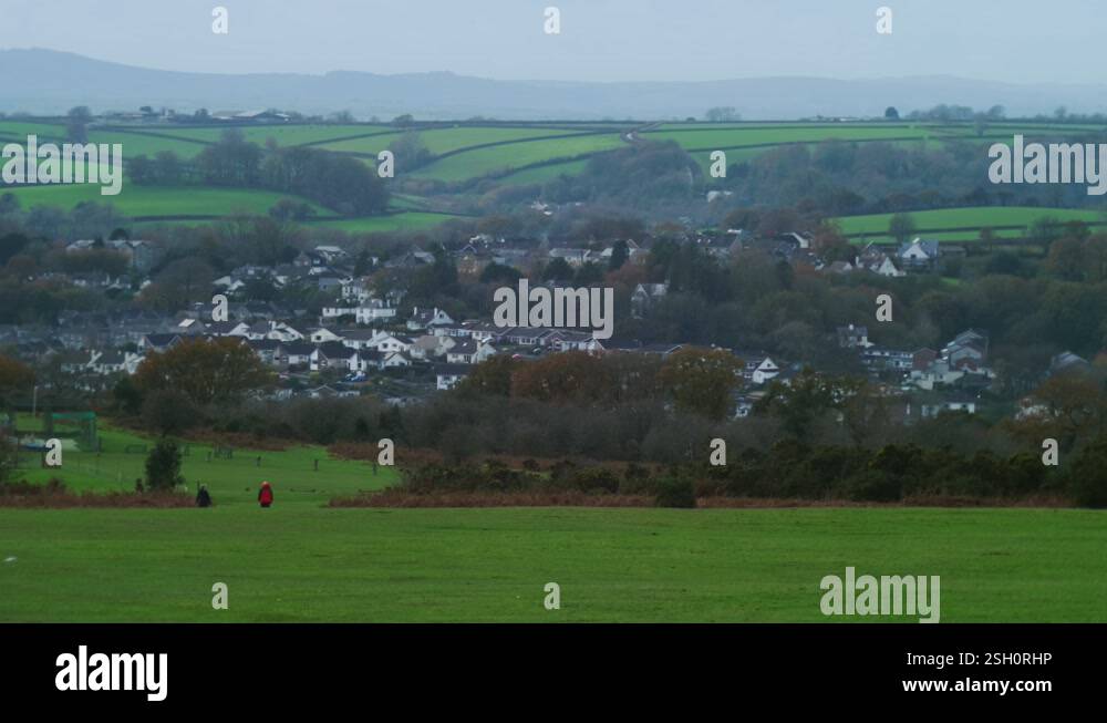 Two hikers walk across moorland grass towards a small country town ...