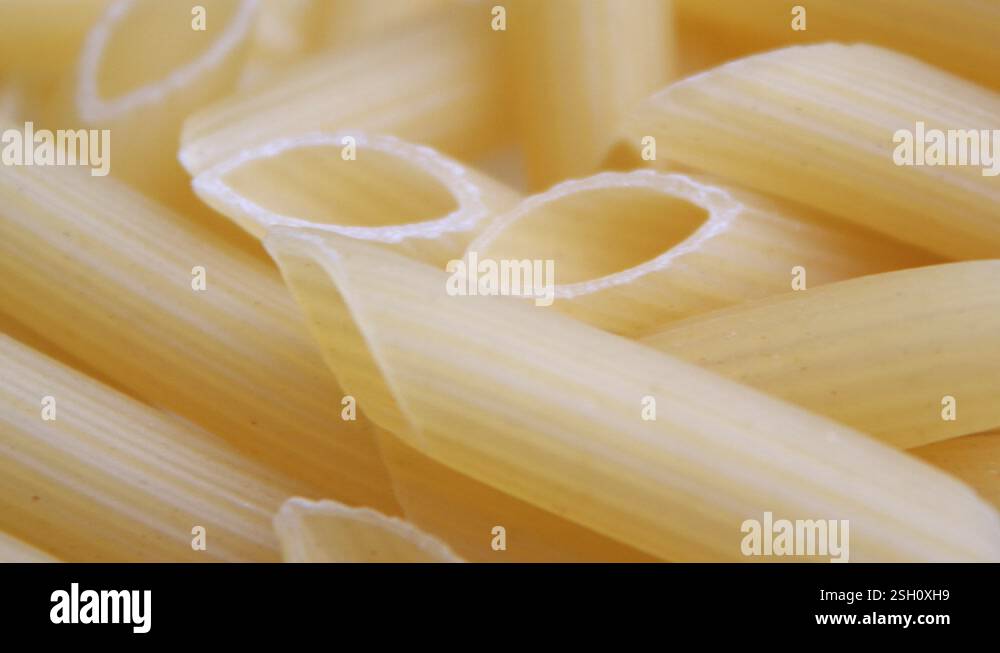 A pile of raw yellow pipe-shaped pasta lies on the surface. Raw pasta ...