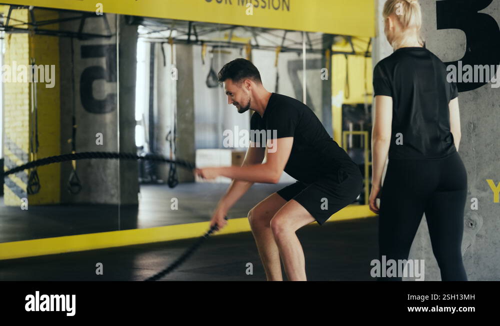 Woman gym trainer explaining man how to do battle rope workout ...