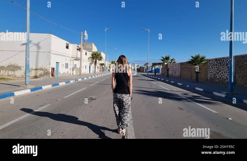woman walks alone on a deserted road in the city of Tarfaya in Morocco ...