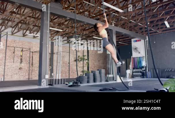 Performing rope climb exercise, strong fit woman training upper body ...