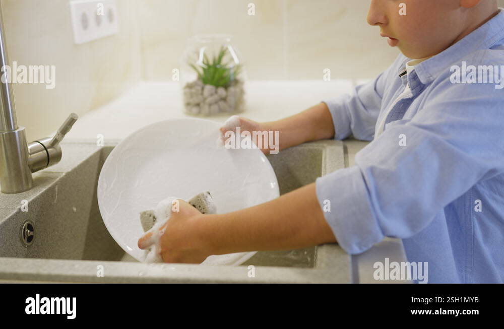 Independent child washing up, using foamy dishwashing detergent ...