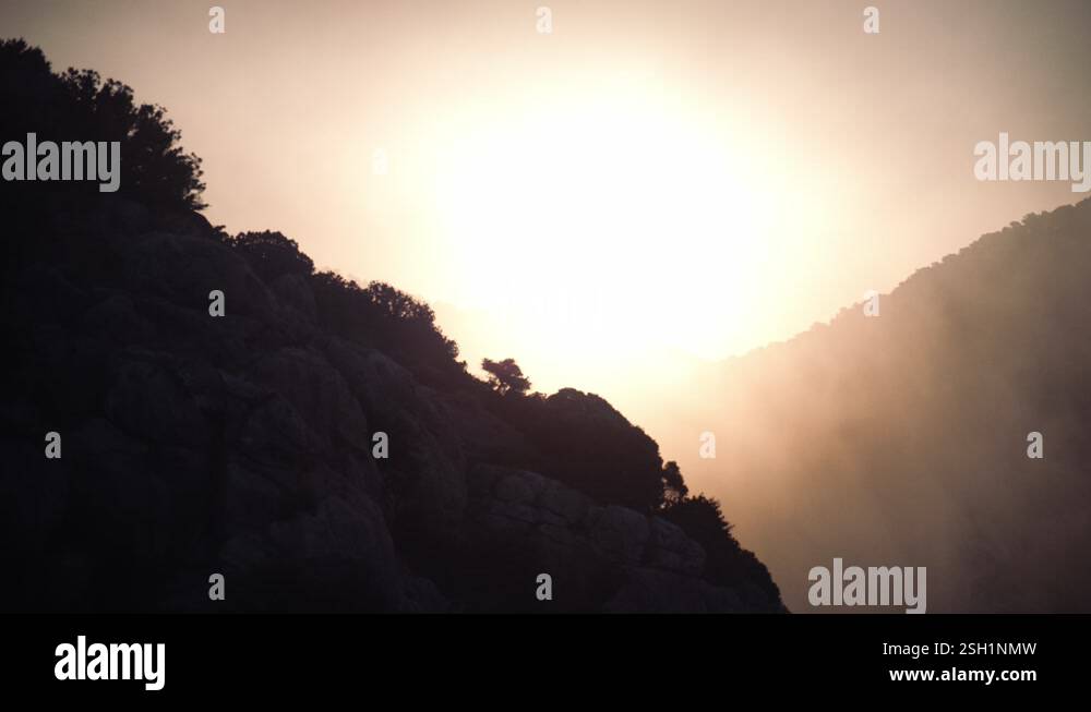 The sun shines through the fast moving clouds on a cliffside on Ibiza ...