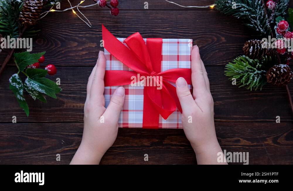 Women's hands take a gift box in a package with a red bow on the table ...