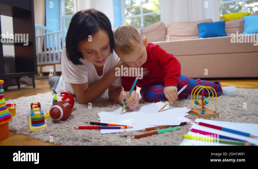 Caring young mum or nanny helping cute kid drawing picture with pencils ...