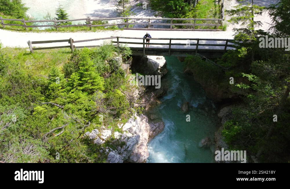 man standing on bridge over fast river rapids in the forest of Italian ...