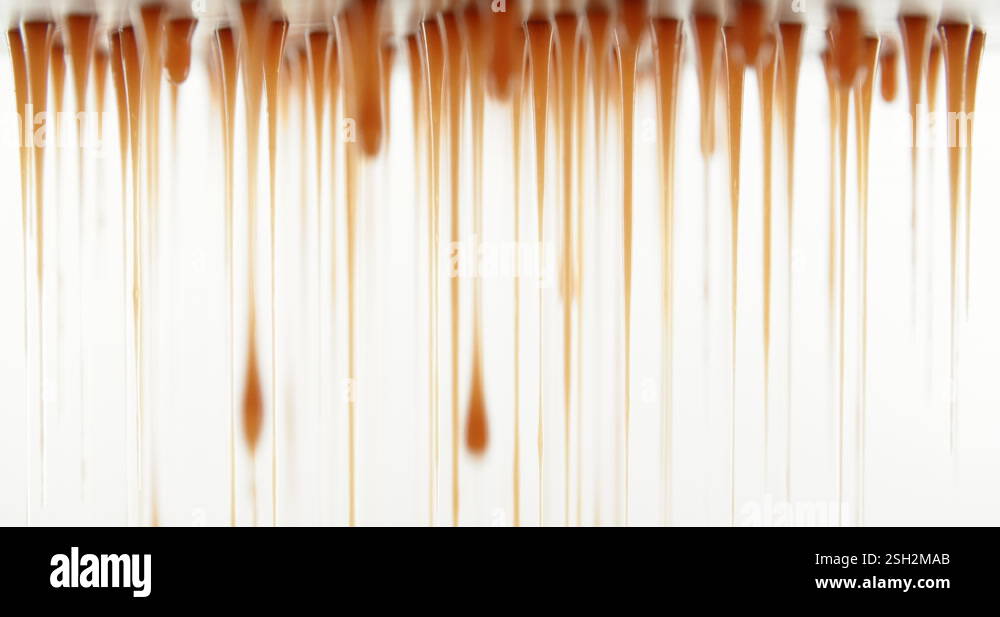 Dripping caramel droplets flowing down liquid sweet sauce on white ...