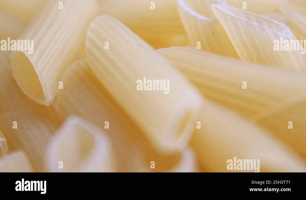 A pile of raw yellow pipe-shaped pasta lies on the surface. Raw pasta ...