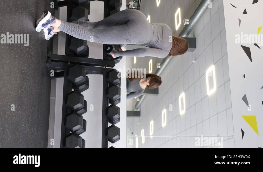 Beautiful slender girl with long hair lifts dumbbells in the gym ...