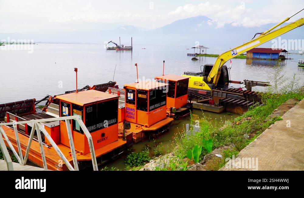 Heavy dredging equipment backhoe and boats docked on lake shore in ...