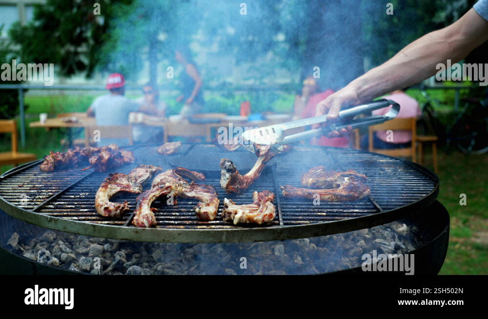 Person preparing meat on grill outside with friends and family in ...
