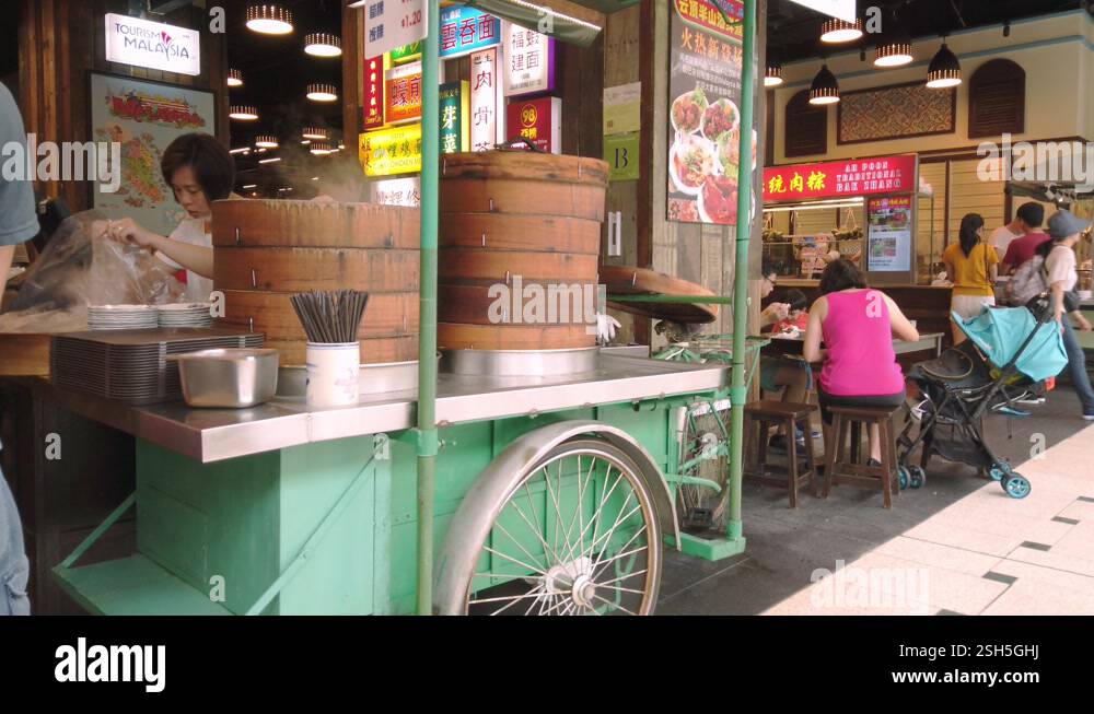 A bun cart selling dimsum in front of a busy food court. A family with ...