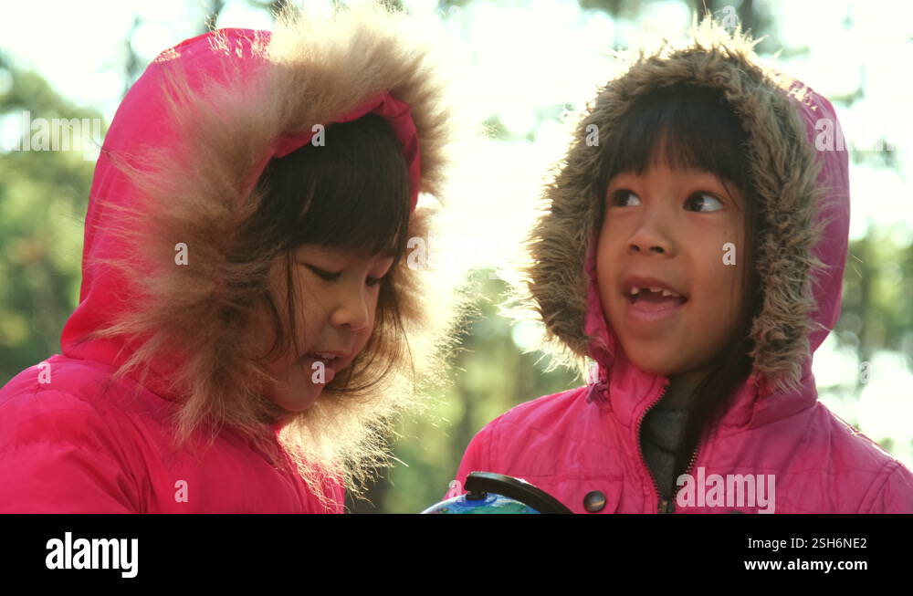 Two cute Asian girls learning a model of the world on nature background ...