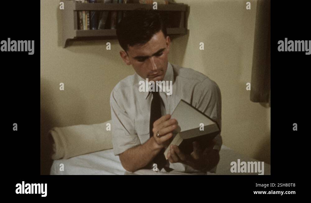 1950s: Man in a uniform sits down on a bunk in a cabin with a book ...