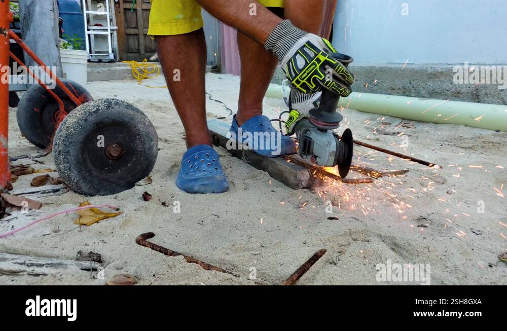 Man cuts rebar holding it with his foot use angle grinder and gloves in ...