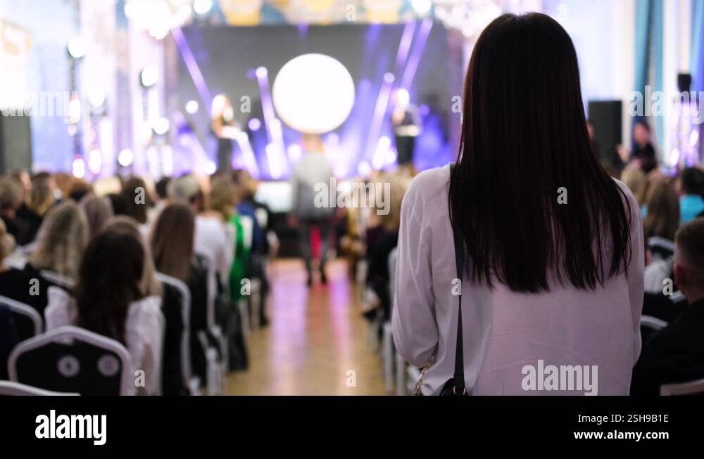Guests in evening attire sit in a spotlighted lobby and look at the stage Stock Video Footage ...