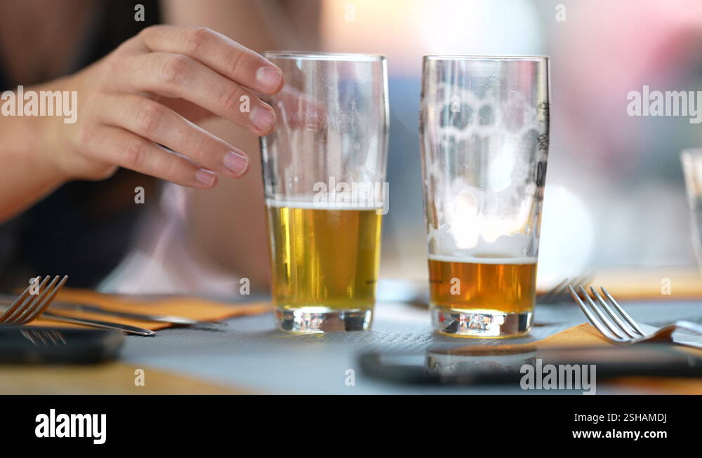 Female hand picking glass of draft beer at restaurant. Two half full ...