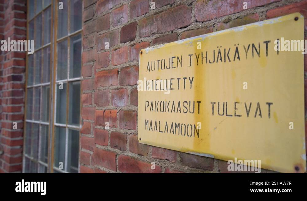An yellow warning sign in Finnish language hanging on an old red brick ...