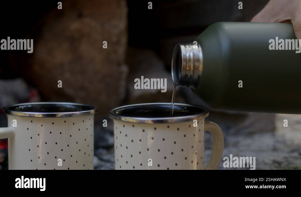 Close up hot boiling water is poured from green thermos into white mug ...