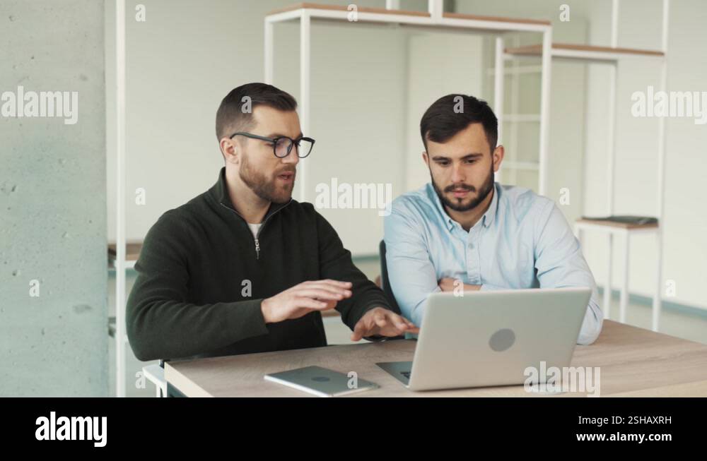 A male mentor is training a young male intern in an office using a ...