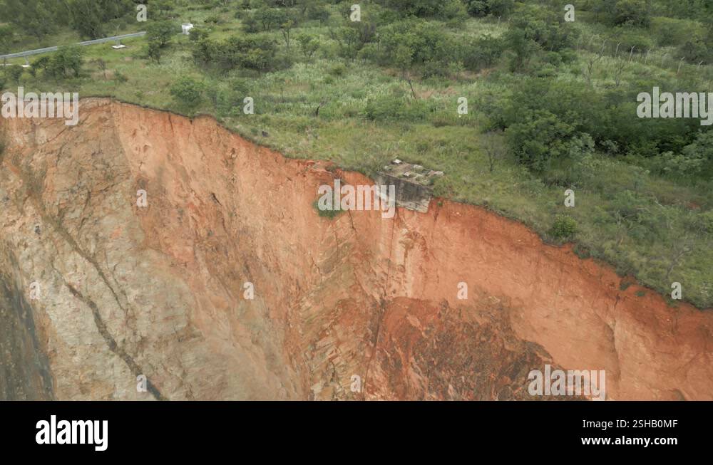 Aerial descends to concrete foundation at edge of vertical rock cliff ...