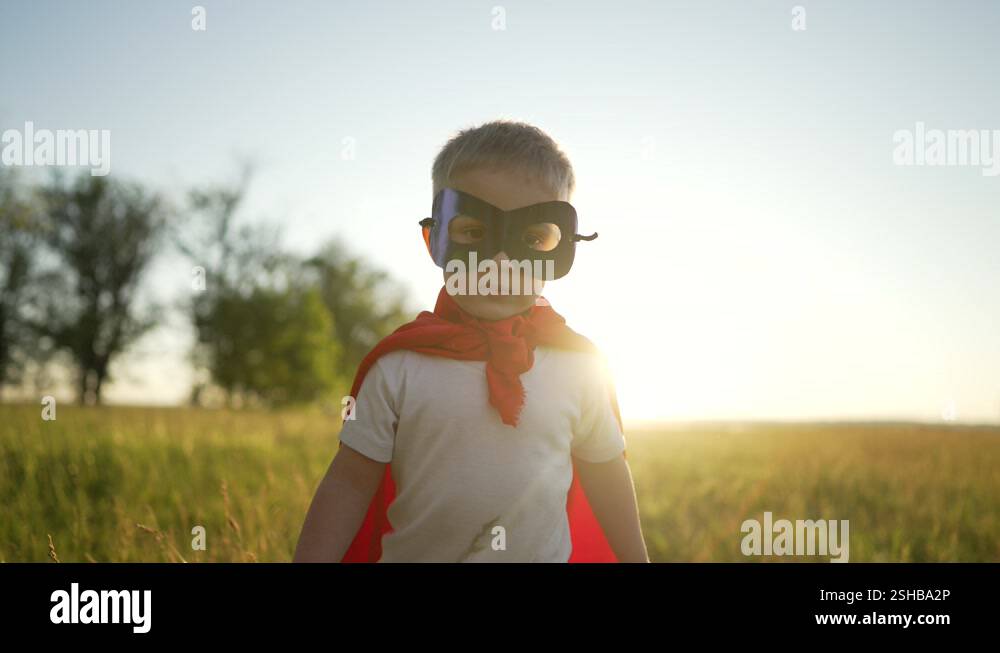Happy child hero runs on green grass. Boy in a red superhero cape ...