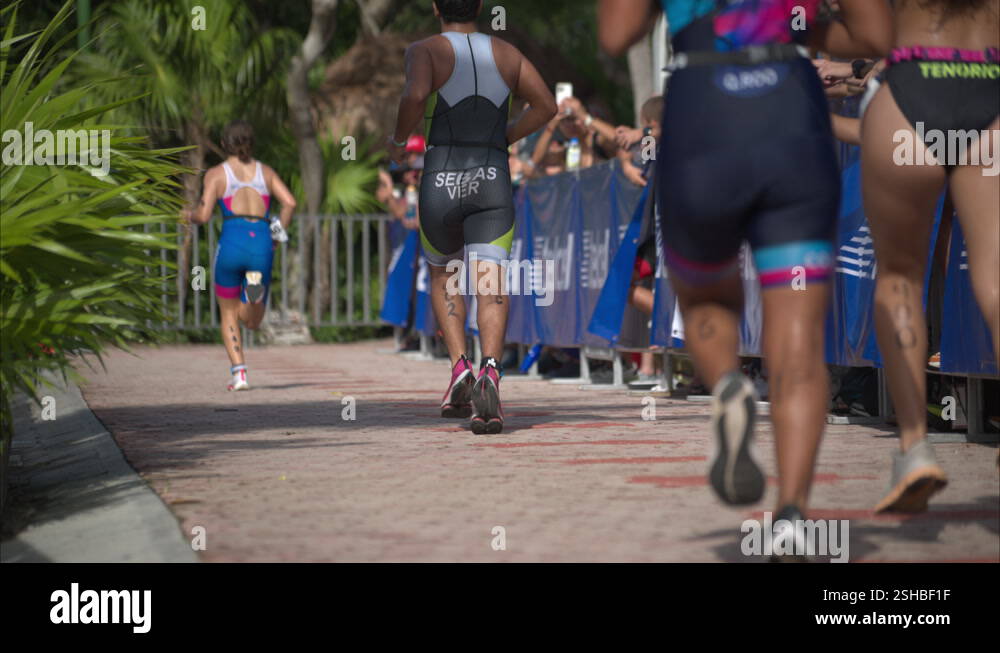 A group of four athletes running passing by a crowd of spectators ...