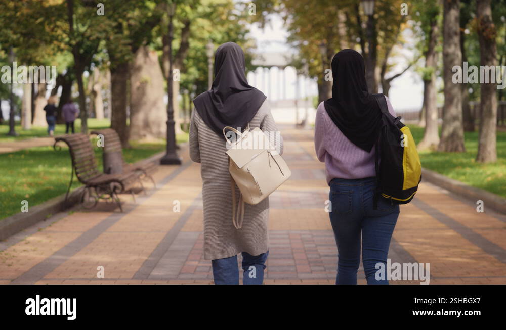 Two muslim female students in hijabs walking campus park and talking ...