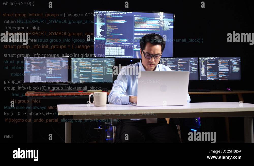 Asian Male Programmer Writing Code By A Laptop Using Multiple Monitors
