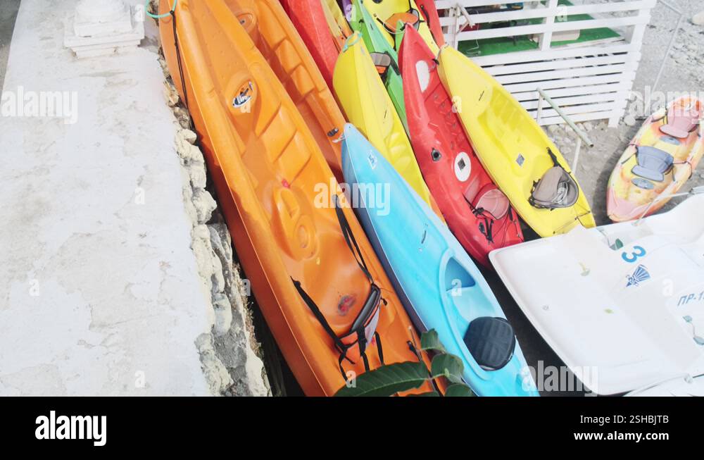 Colorful kayaks stand vertically on the seashore. Canoe rental, kayak ...