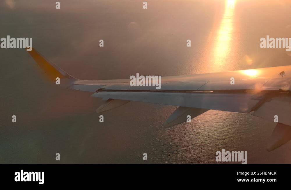 Backlight of an airplane wing at sunset while the plane maneuvers over ...