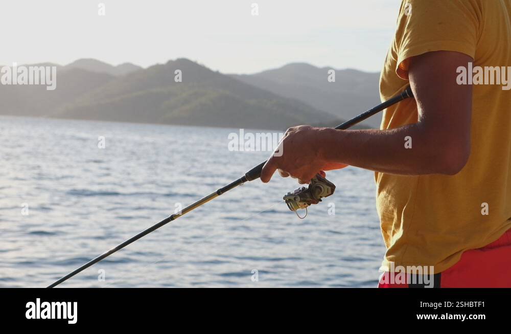 Young man fishing on a lake with spinning rod from the boat at sunset ...