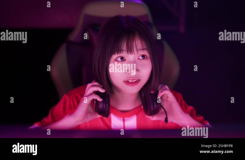 Handheld, portrait of a asian female gamer in headphones, plays a video ...