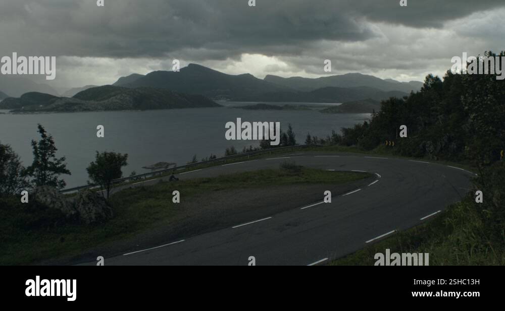 Young man cycling uphill in dark, moody, windy weather, storm brewing ...