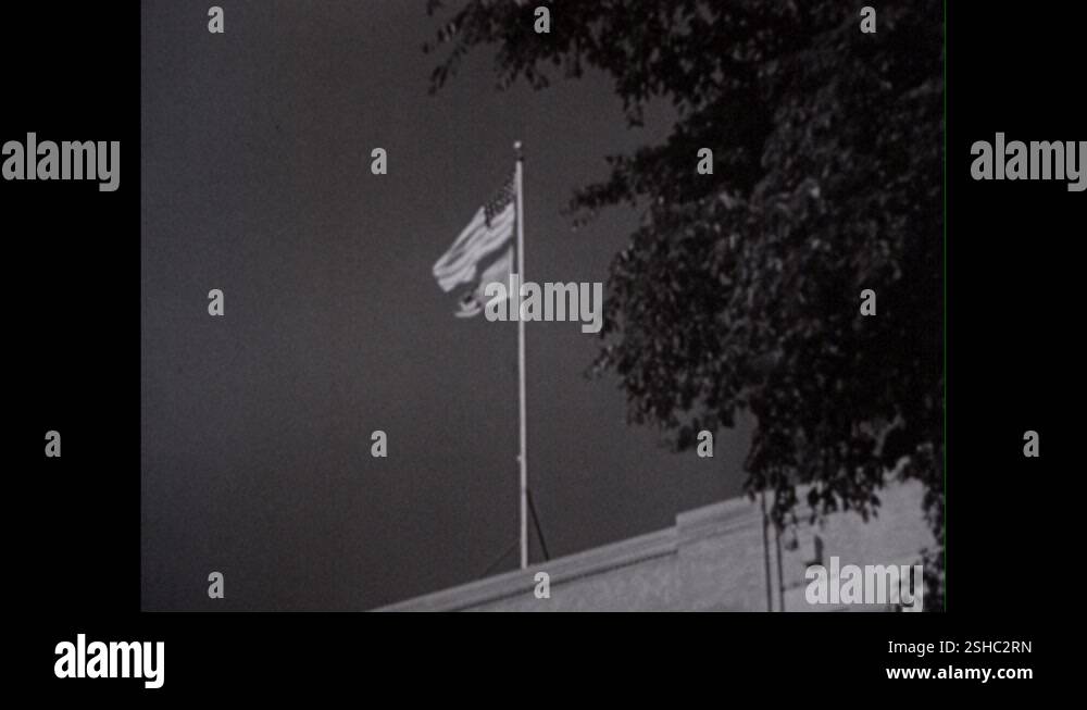 1940s: Workers assemble engine parts in factory. American flag flies ...