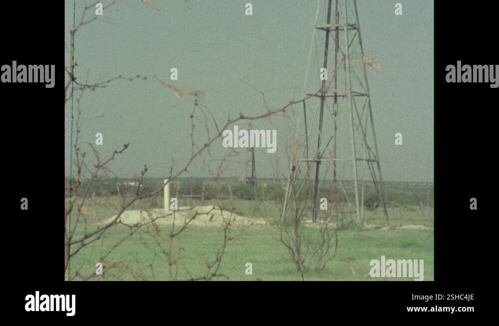 1970s: Tree branches sway in wind. Oil well, tall platform, machinery ...