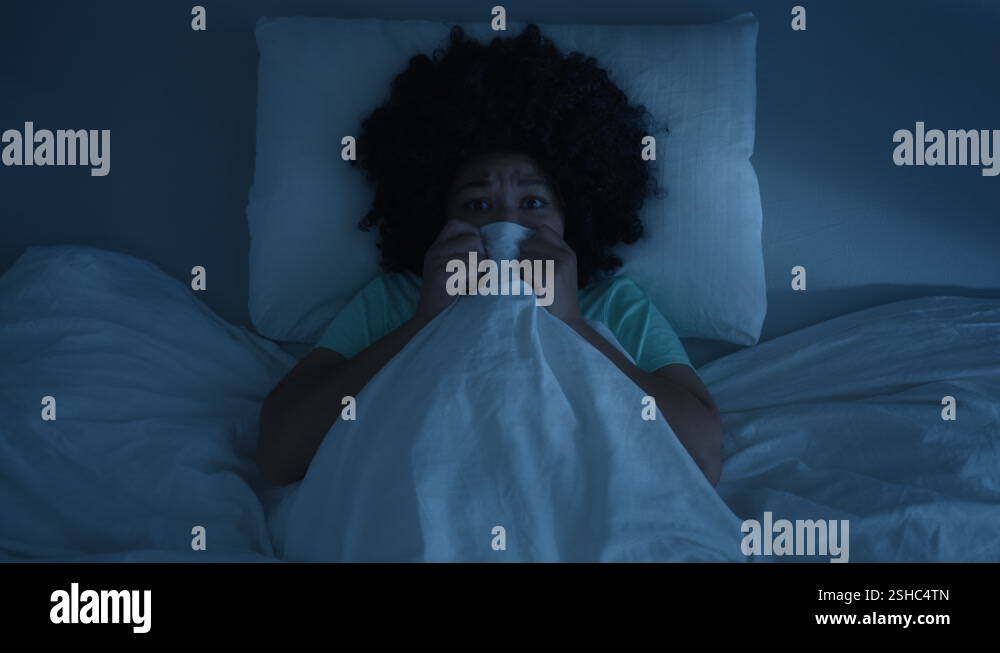 Woman of color lying in bed and covering face by blanket to not see ...