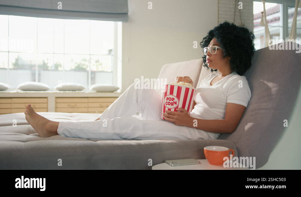 Attractive african american woman sitting on couch sofa with popcorn at ...