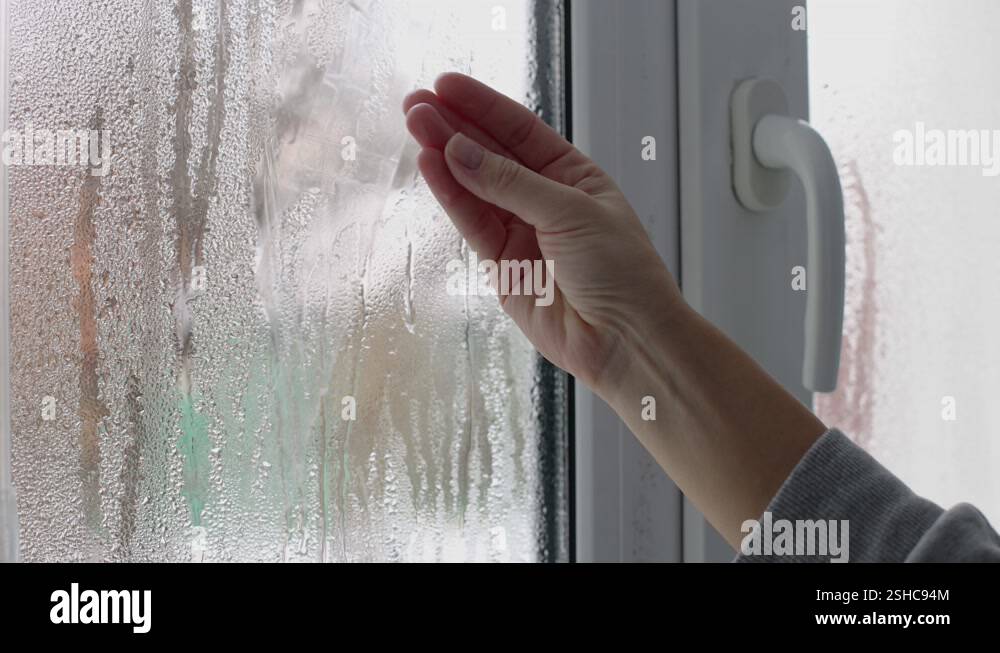 A womans hand touching wet window glass with water drops of ...