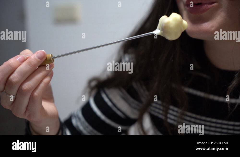 Young cute girl eating fondue, a Swiss melted cheese dish served in a ...